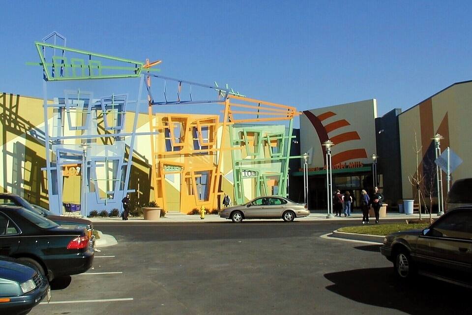 Um estacionamento com carros, um edifício com uma grande placa e uma estrutura colorida ao fundo.