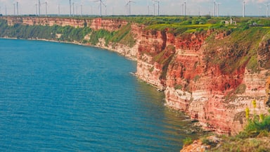 Paisagem costeira com falésias, um corpo d'água e turbinas eólicas ao longe.