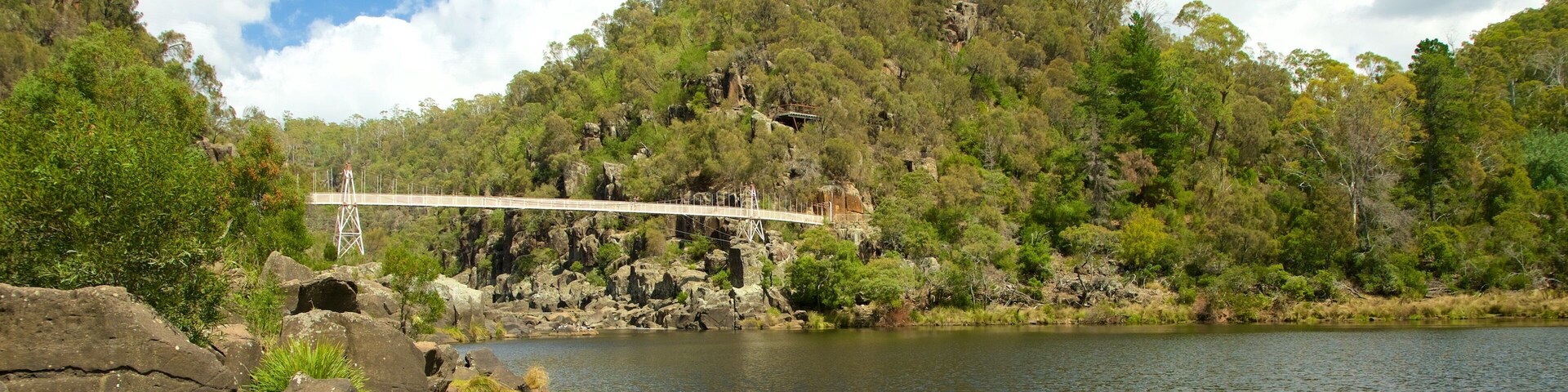 Uma ponte sobre um rio com margens rochosas e floresta densa ao fundo.
