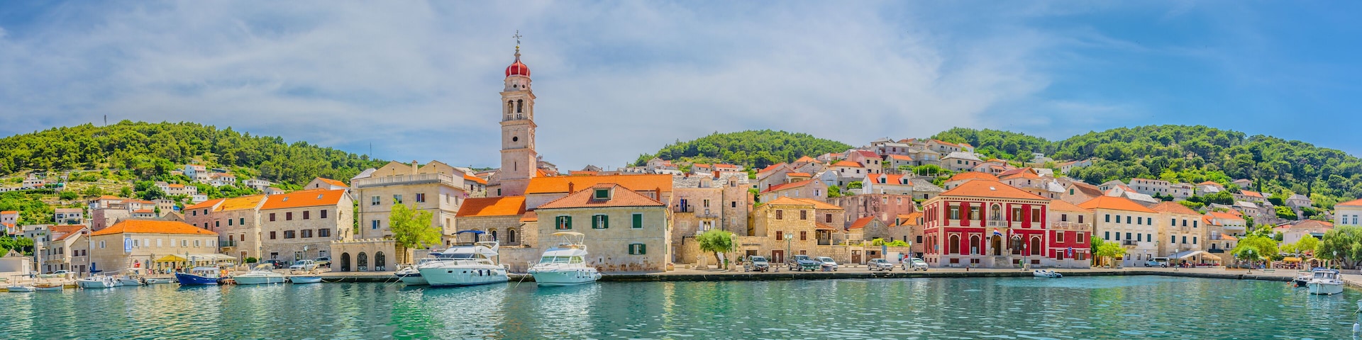Uma cidade costeira com edifícios históricos, uma torre imponente e barcos atracados na orla.