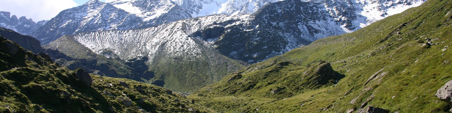 Paisagem montanhosa com rio corrente, terreno rochoso e picos nevados.