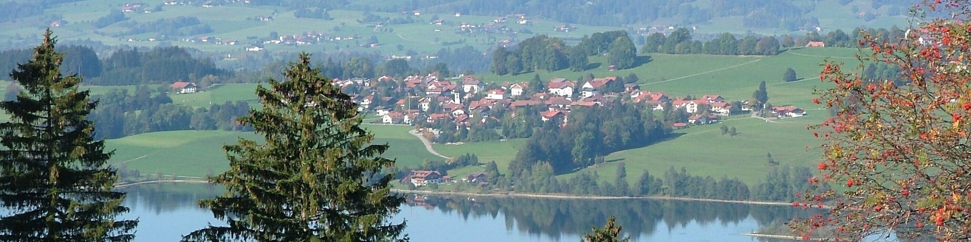 Um lago cercado por uma aldeia e colinas arborizadas.