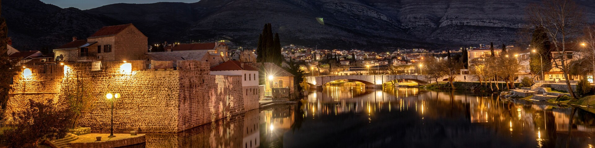 Uma cidade histórica com um rio refletindo edifícios e uma montanha ao fundo.