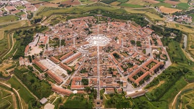Vista aérea de uma cidade histórica murada com uma praça central, rodeada por campos agrícolas e um rio.