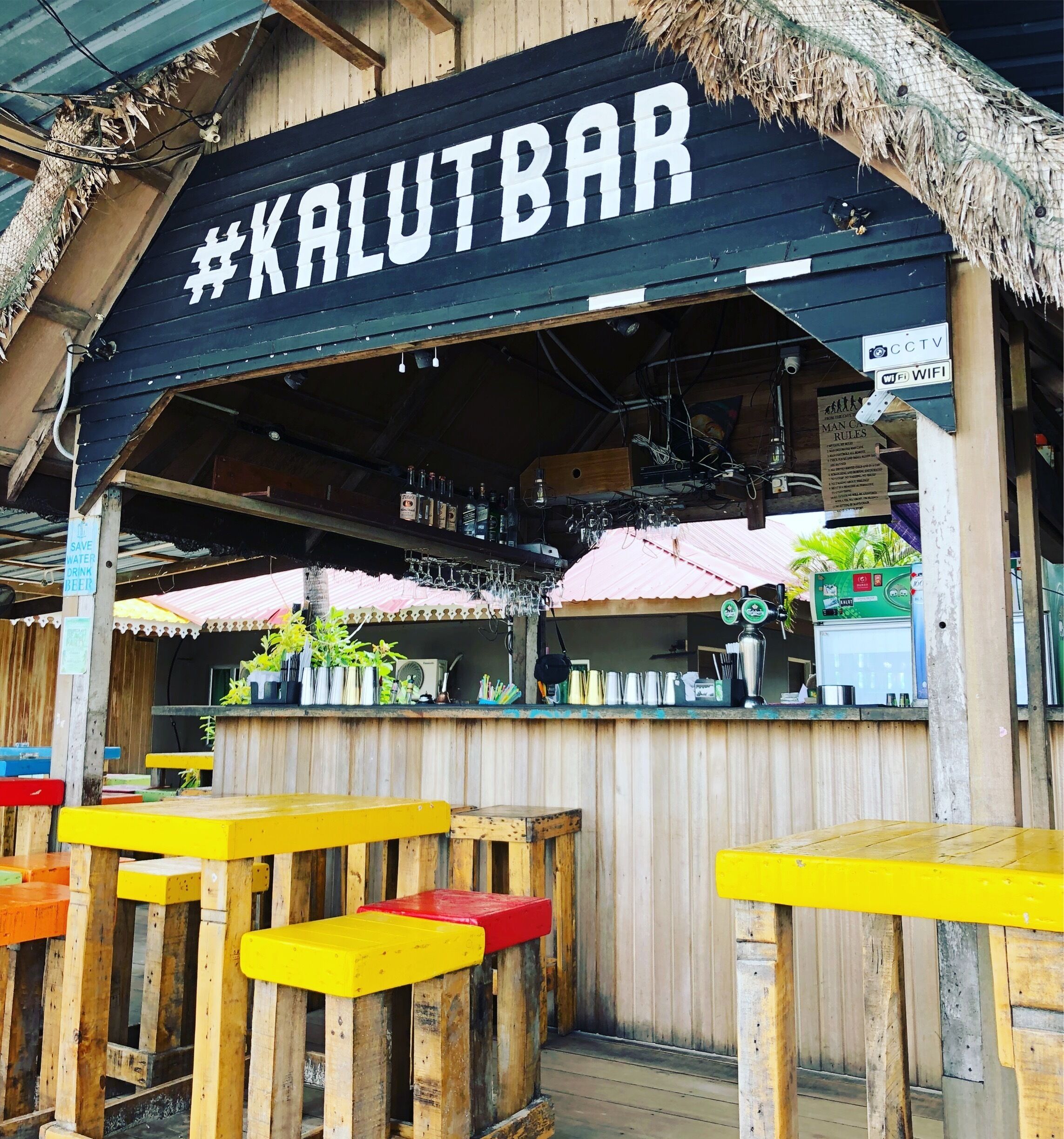 Um #KALUTBAR com mesas de madeira e um telhado de palha.