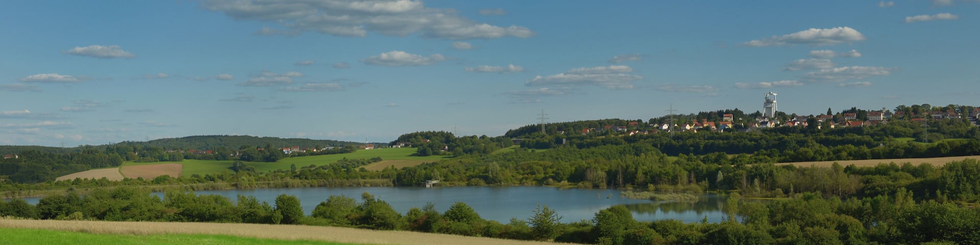 Schlammweiher Hahnwies der ehemaligen Grube Göttelborn, Blick von Steinertshaus Richtung Damm. Heute Teil der Landschaft der Industriekultur Nord (LIK.Nord), Naturschutzgroßprojekt, Landschaftslabor Vogelzug und wilde Weiden. Im Hintergrund ist das Fördergerüst Schacht IV ("Weißer Riese") der ehemaligen Grube Göttelborn zu sehen (2017).