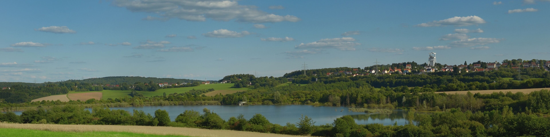 Schlammweiher Hahnwies der ehemaligen Grube Göttelborn, Blick von Steinertshaus Richtung Damm. Heute Teil der Landschaft der Industriekultur Nord (LIK.Nord), Naturschutzgroßprojekt, Landschaftslabor Vogelzug und wilde Weiden. Im Hintergrund ist das Fördergerüst Schacht IV ("Weißer Riese") der ehemaligen Grube Göttelborn zu sehen (2017).