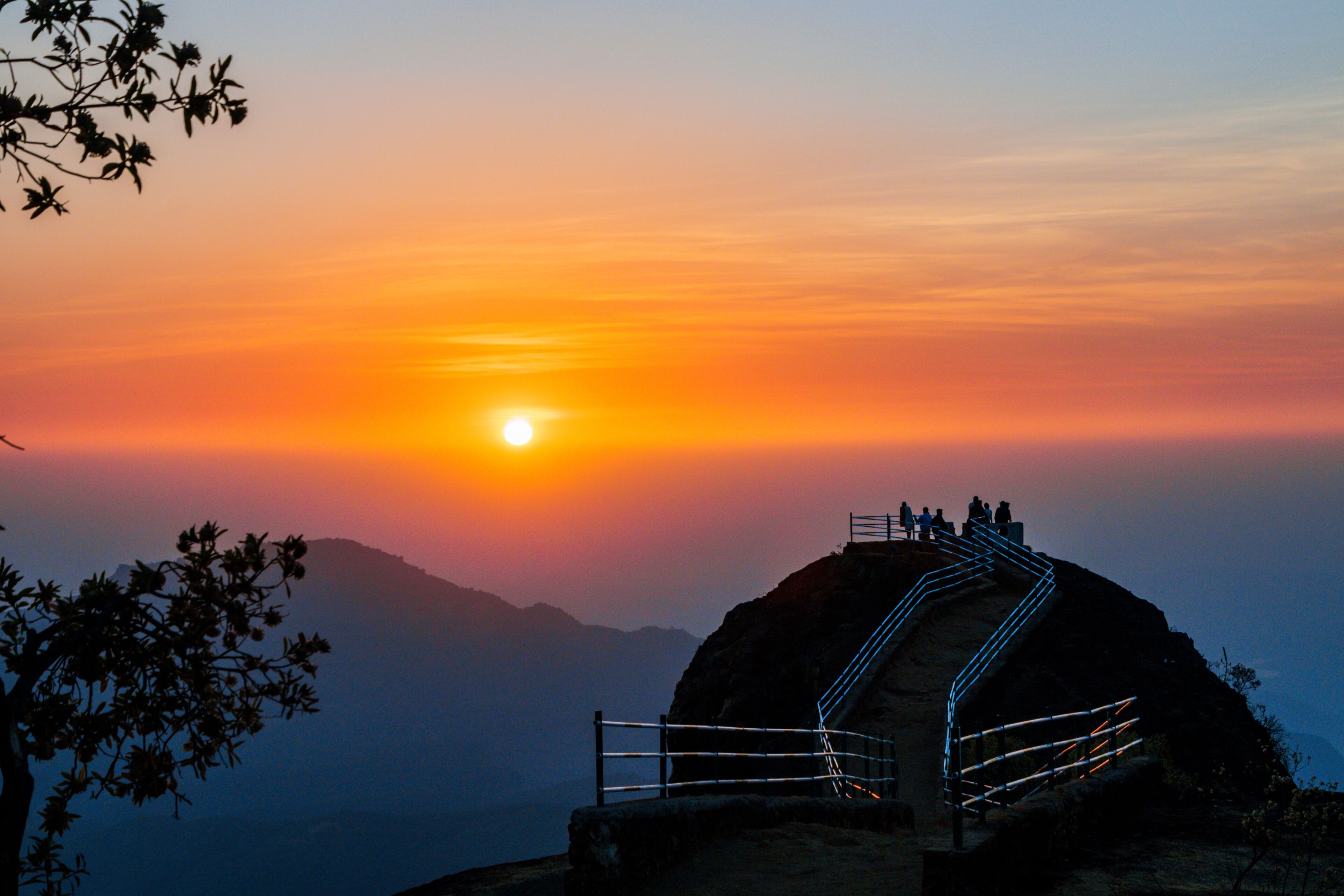 Pôr do sol sobre uma paisagem montanhosa com uma plataforma de observação e uma escadaria que a leva.