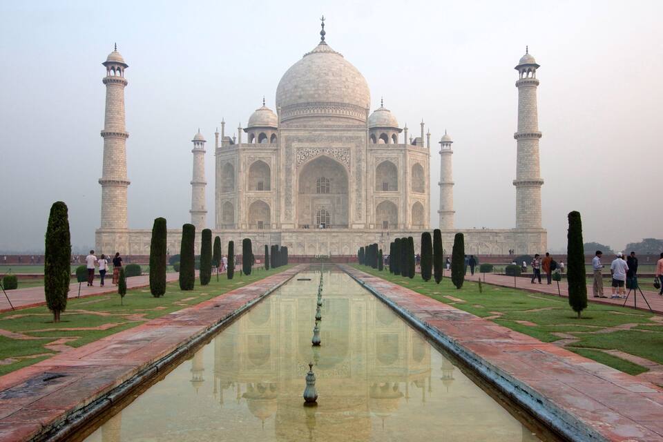 O Taj Mahal com seu reflexo na água, quatro minaretes e um jardim simétrico.