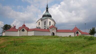 Uma igreja com cúpula verde e telhado vermelho, cercada por grama e árvores.