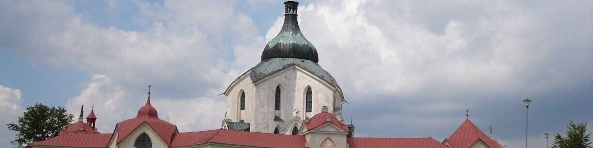 Uma igreja com cúpula verde e telhado vermelho, cercada por grama e árvores.