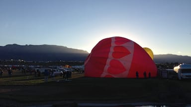Uma grande balão de ar quente vermelha e amarela com padrão de folha, com montanhas e céu azul ao fundo.