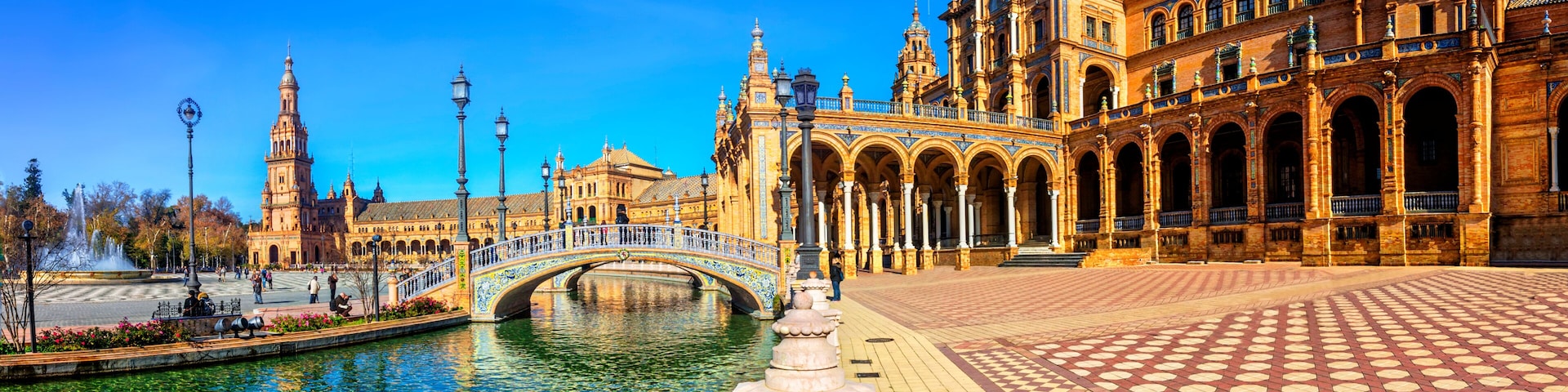 Um edifício histórico com arquitetura elaborada, céu azul límpido e uma ponte sobre águas calmas.