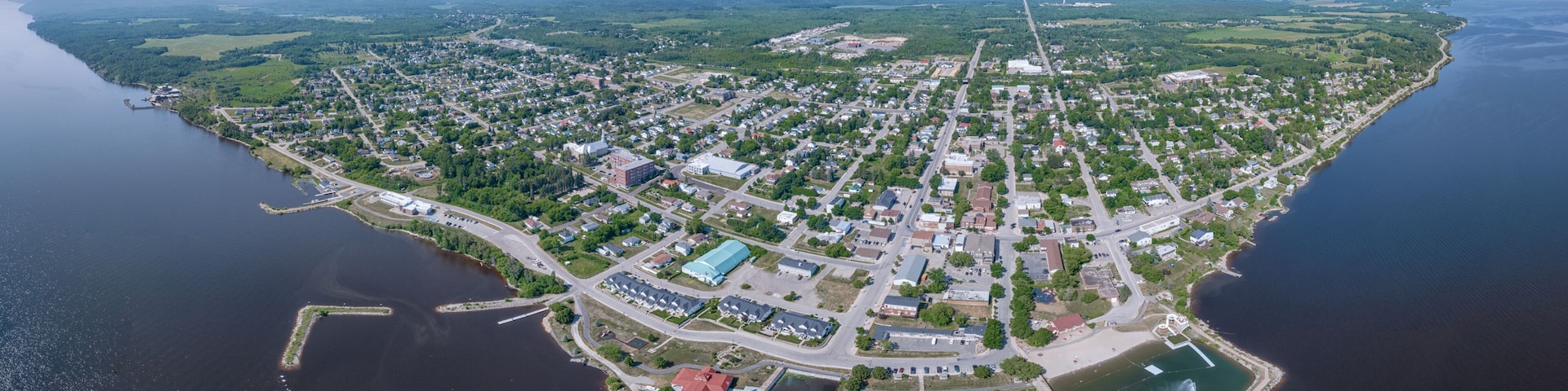 Vista aérea de uma cidade costeira com um porto de iates, área residencial densa e vegetação ao redor.