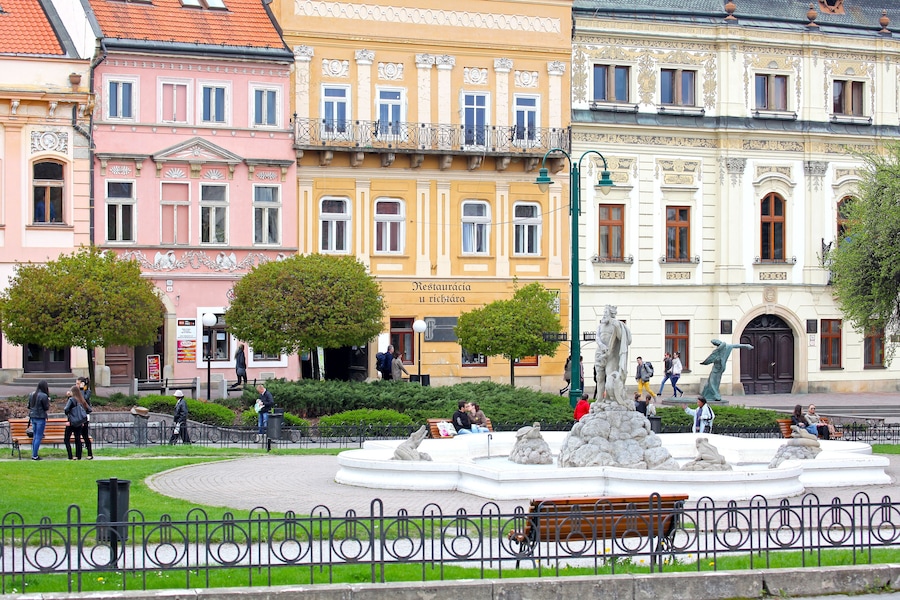 Uma praça pública com uma fonte, bancos e pessoas.