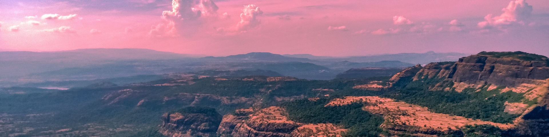 Paisagem montanhosa com formações rochosas em camadas e vegetação verde densa.