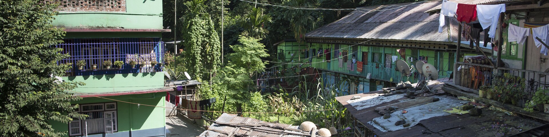 Uma aldeia rural com casas tradicionais, um edifício verde com telhado de azulejos e uma área cercada com roupa pendurada.