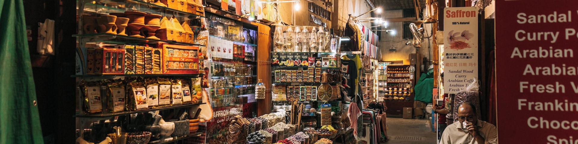 Uma rua de mercado estreita, com diversas lojas vendendo especiarias, frutas secas e outros produtos.