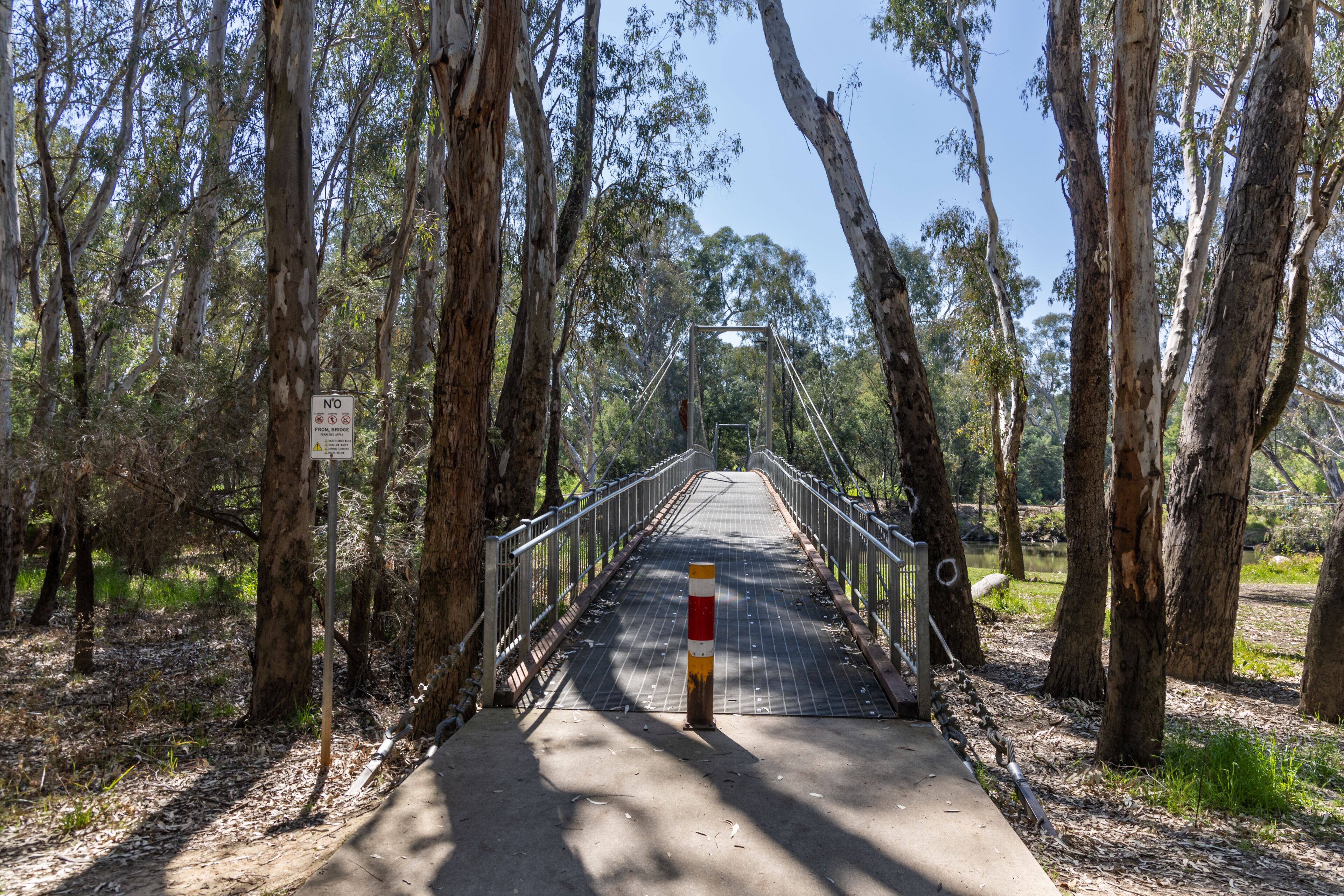 Uma ponte para pedestres numa floresta, com árvores e uma placa de 'Proibido o Acesso'.