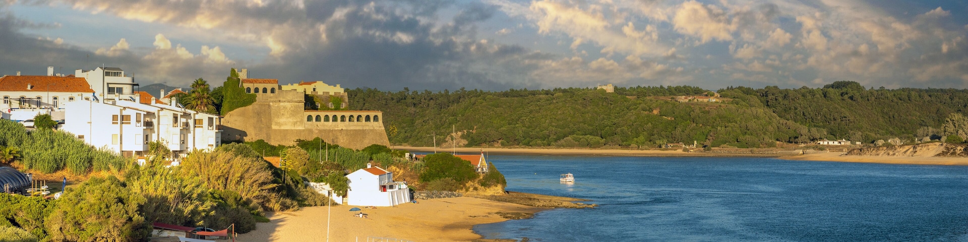 Uma vila costeira com praia, um cais e uma construção que lembra um castelo.