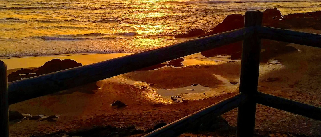 Um pôr do sol sobre uma praia com uma passarela de madeira.