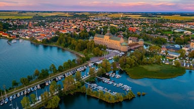 Uma cidade à beira de um lago, com um castelo imponente, marina e vegetação ao redor.