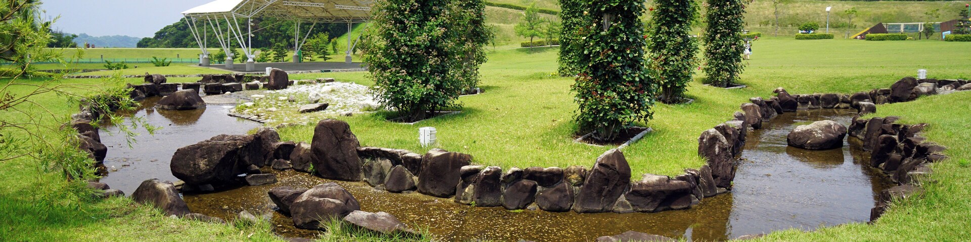 Um jardim arborizado com lago, pedras e árvores.
