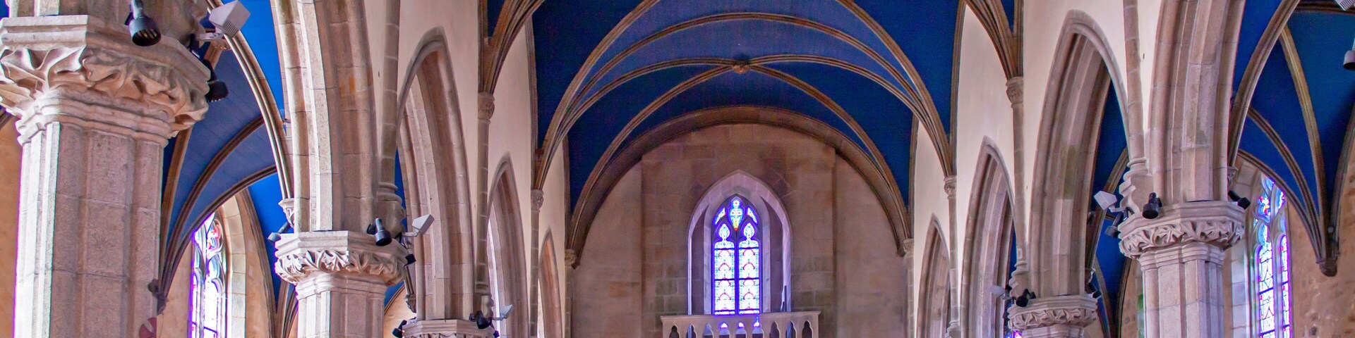 Interior de catedral com altos tetos abobadados, janelas em arco e fileiras de bancos de madeira.