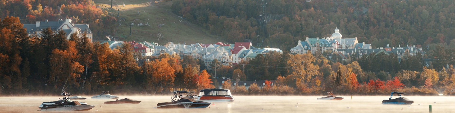 Uma cidade à beira-lago com folhagem de outono, barcos e uma igreja no alto de uma colina.