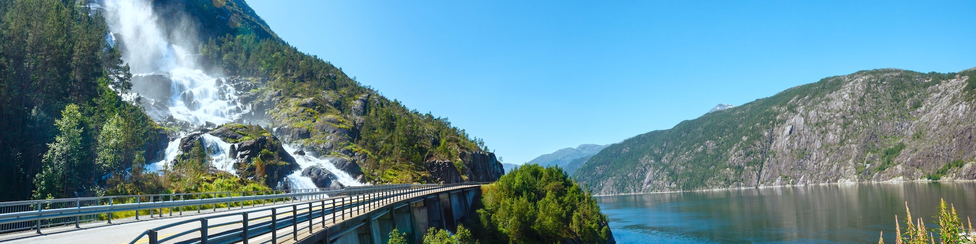 Uma ponte sobre um rio com cachoeiras e paisagem montanhosa.