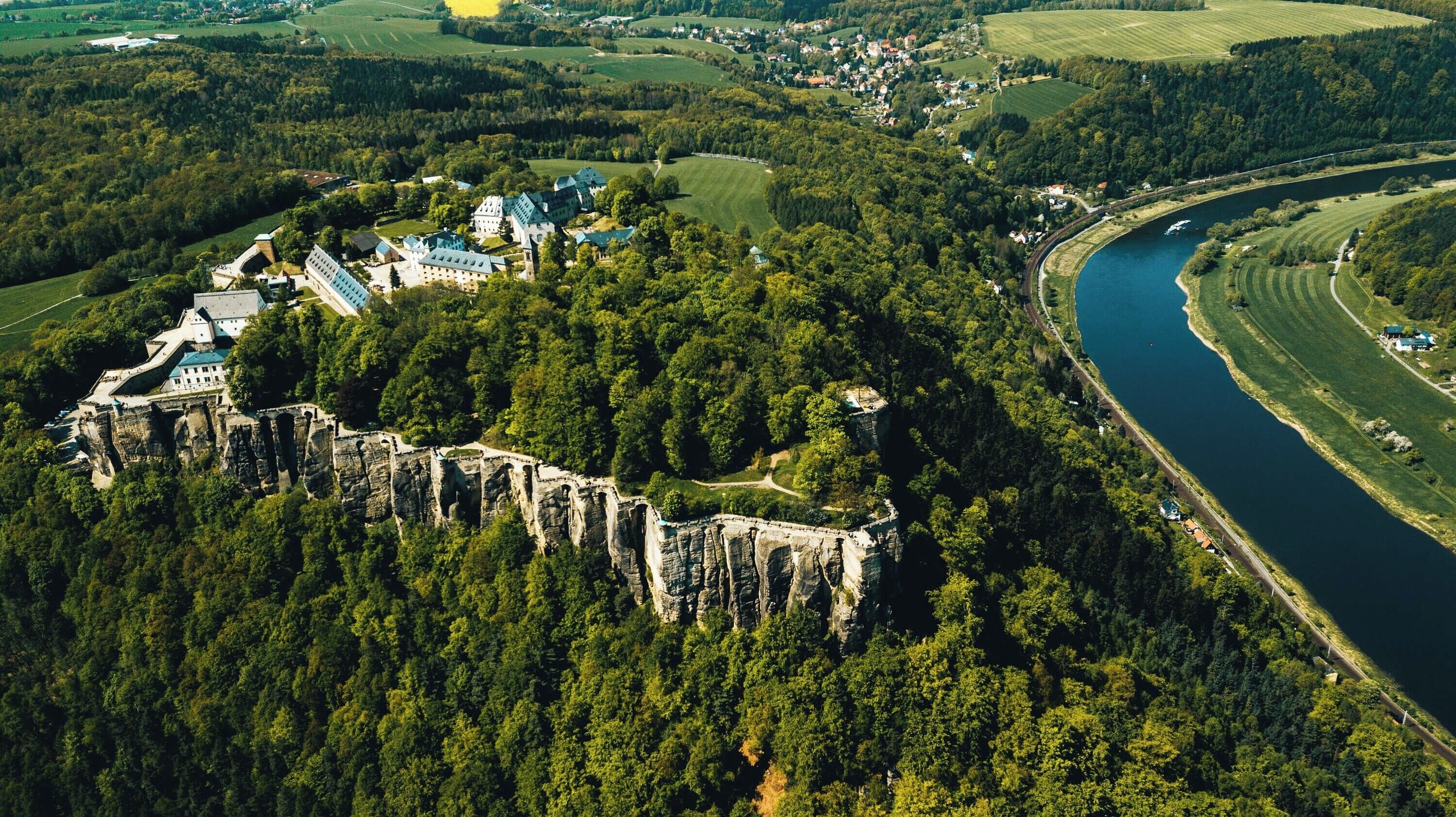 Um castelo rodeado por floresta e um rio.