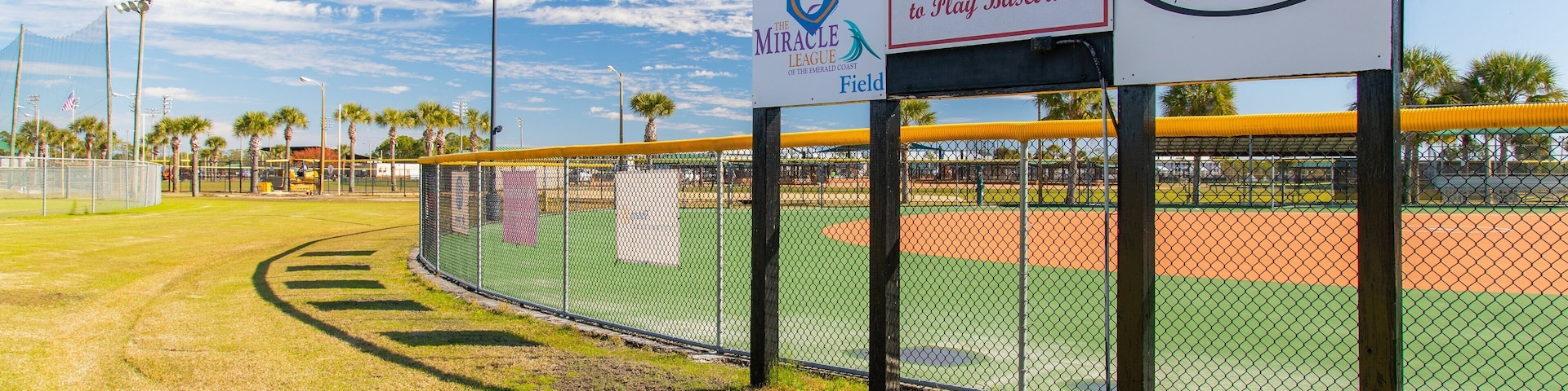 Um campo de beisebol com uma placa de boas-vindas ao campo The Miracle League da Emerald Coast.