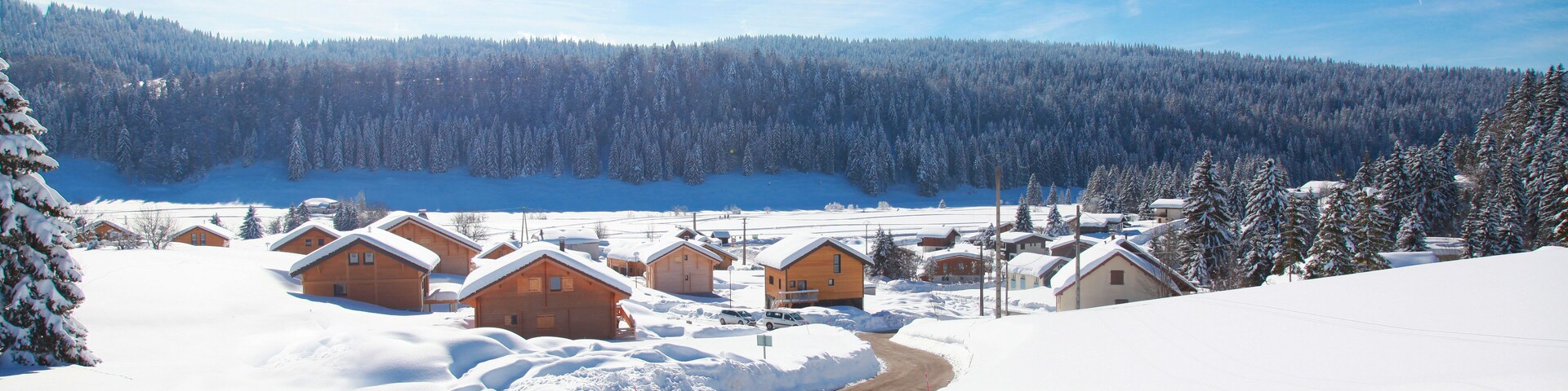 Uma aldeia coberta de neve, com casas de madeira e um céu azul límpido.
