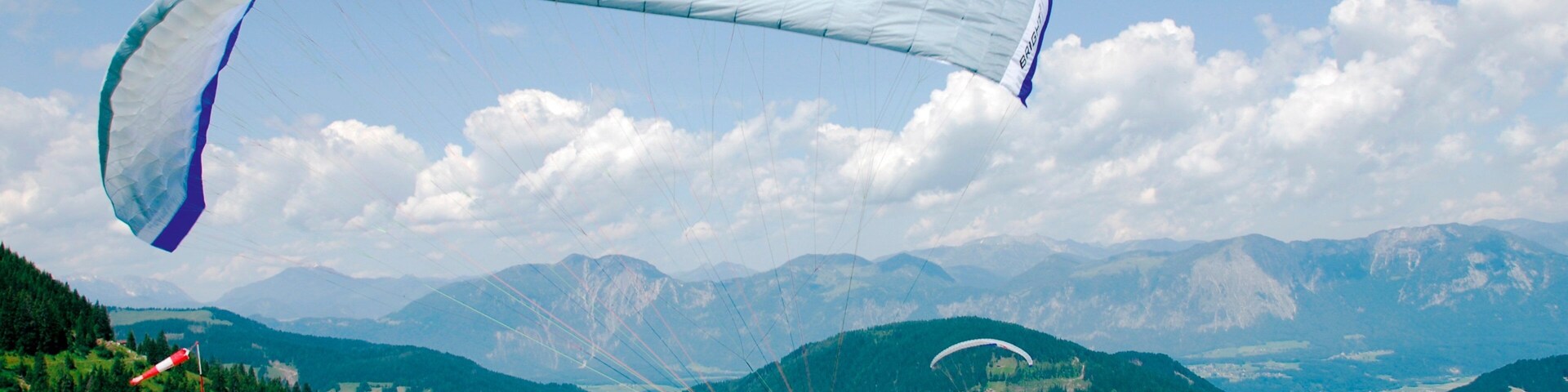 Um parapentista descendo uma colina gramada, com uma paisagem montanhosa ao fundo.