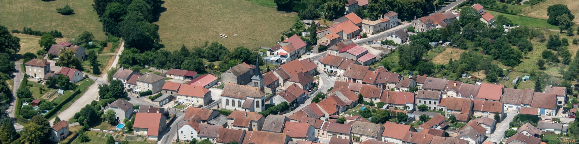 Vista aérea de uma pequena aldeia com casas de telhados vermelhos, campos verdes e uma igreja.