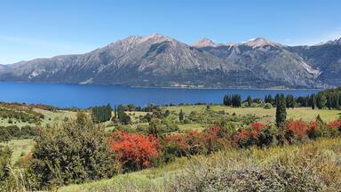 Um lago rodeado por montanhas e árvores com cores outonais.