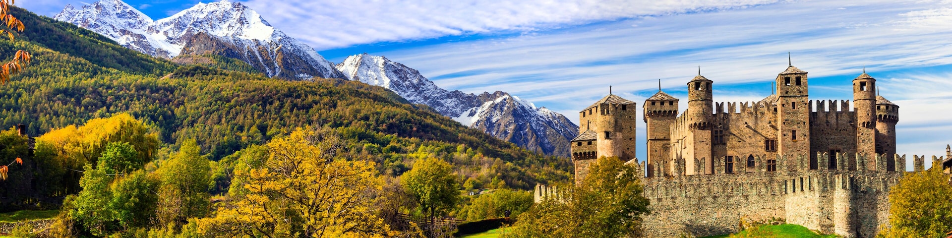 Um castelo rodeado por montanhas e folhagem outonal.