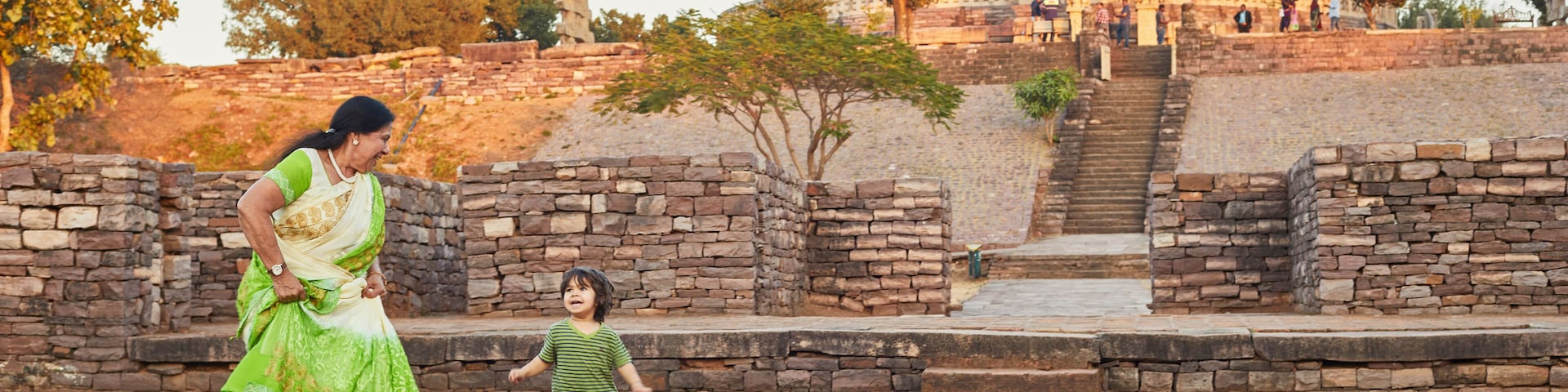 Um local histórico com um grande edifício em forma de cúpula, muros de pedra e uma área pavimentada onde uma mulher e uma criança caminham.