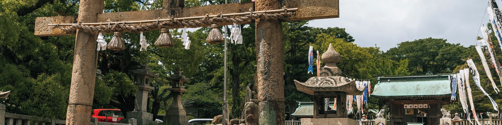 Um portão torii de pedra que dá acesso a um santuário, com uma pequena pagoda e um edifício tradicional ao fundo.