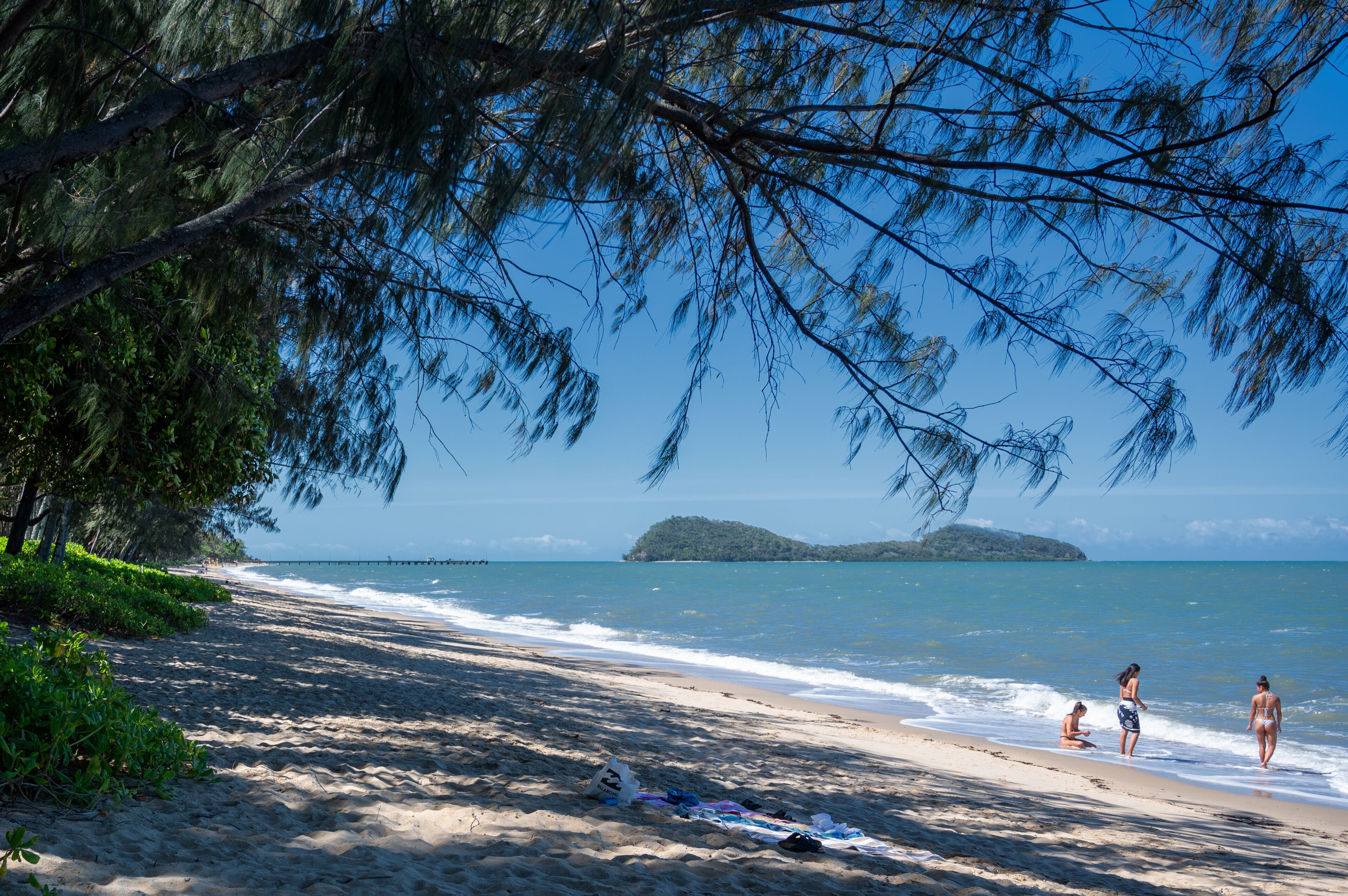 Uma praia com águas azul-claras, uma costa arenosa e uma pequena ilha ao longe.