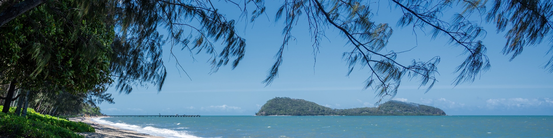 Uma praia com águas azul-claras, uma costa arenosa e uma pequena ilha ao longe.