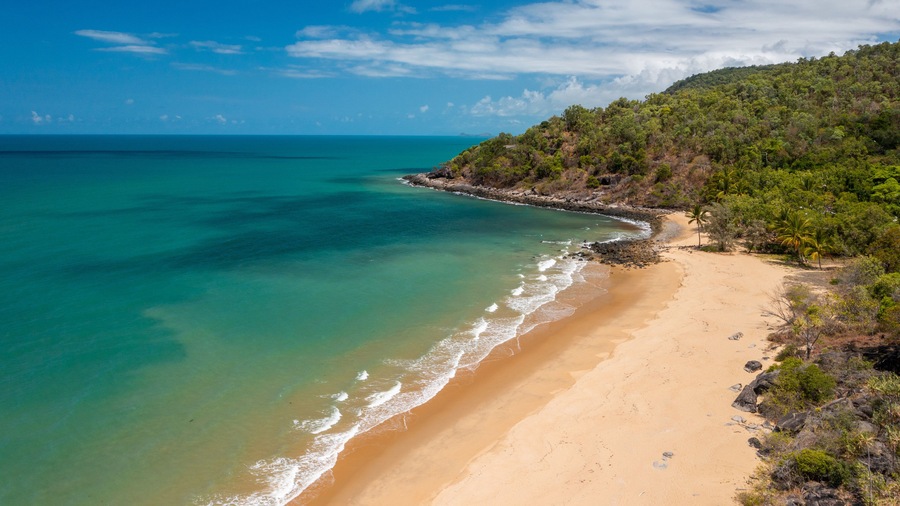 Uma praia com águas azul-turquesa cristalinas, areal arenoso e um morro coberto de vegetação.
