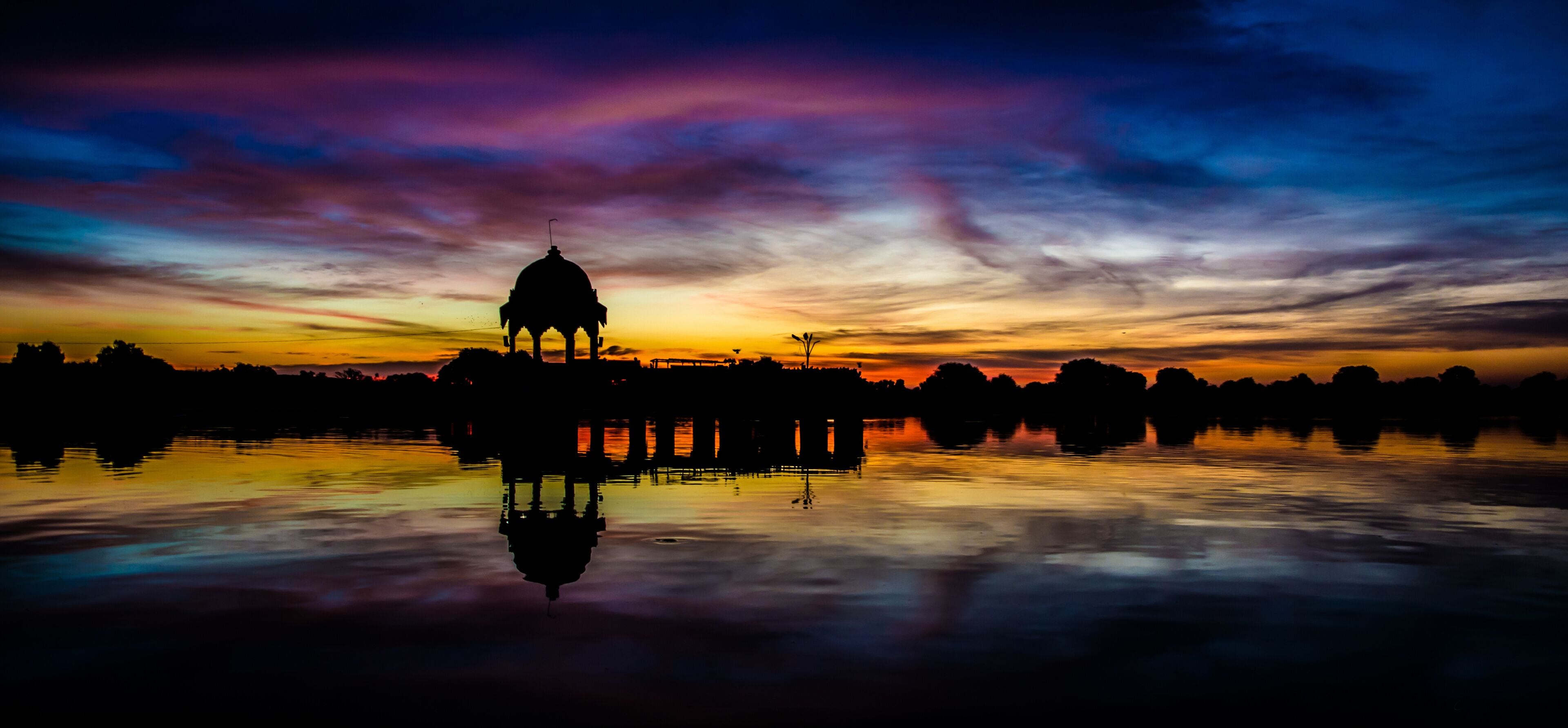 Um pôr do sol sobre a água, com a silhueta de uma estrutura em forma de cúpula.