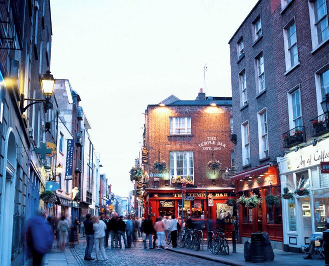Rua de paralelepípedos com edifícios históricos, incluindo The Temple Bar e uma cafeteria.