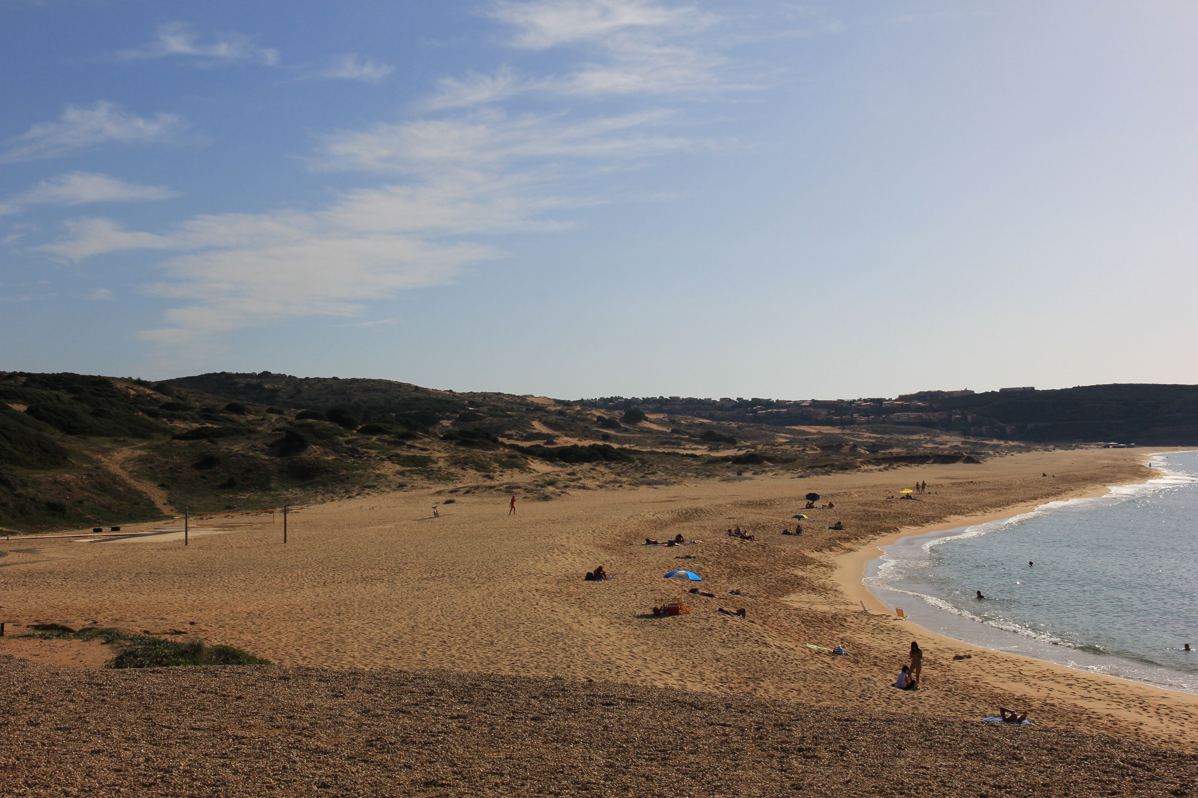 Uma praia arenosa com pessoas tomando sol e nadando, cercada por colinas.