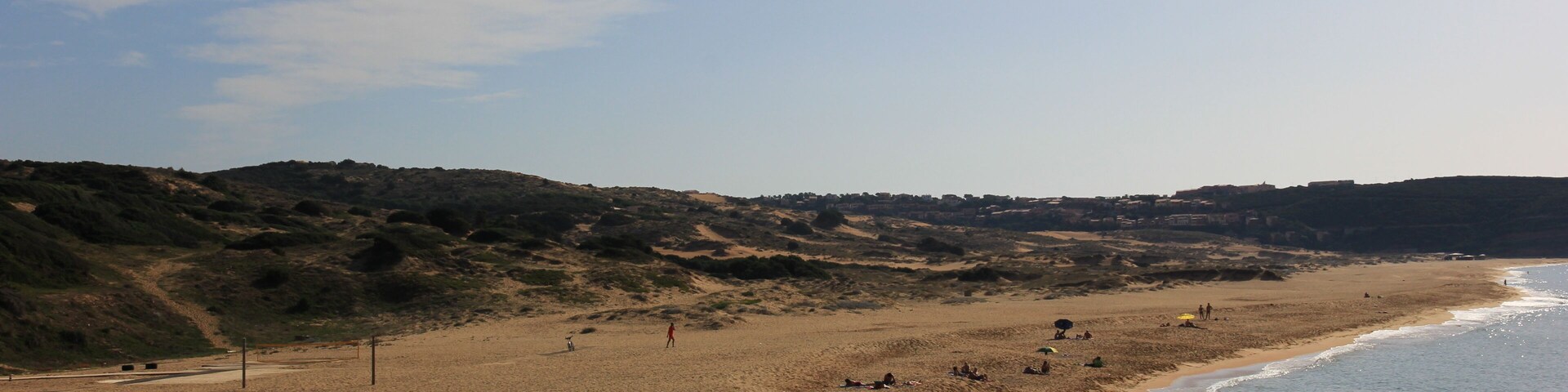 Uma praia arenosa com pessoas tomando sol e nadando, cercada por colinas.