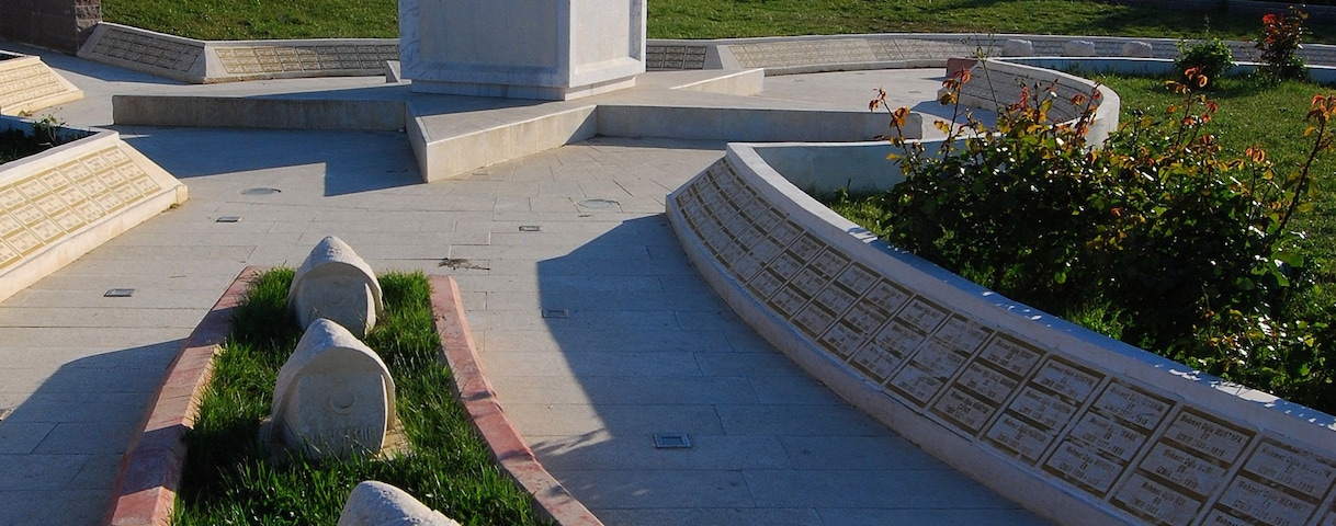 Um monumento com topo pontiagudo, cercado por área ajardinada com grama e calçada pavimentada.