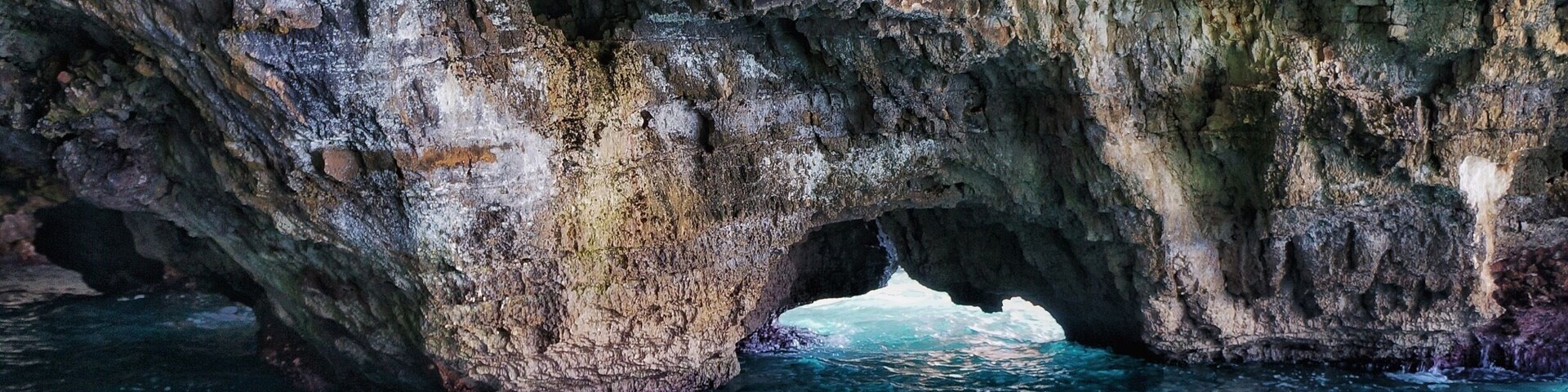 Formação rochosa natural com uma entrada de caverna e água azul cristalina.