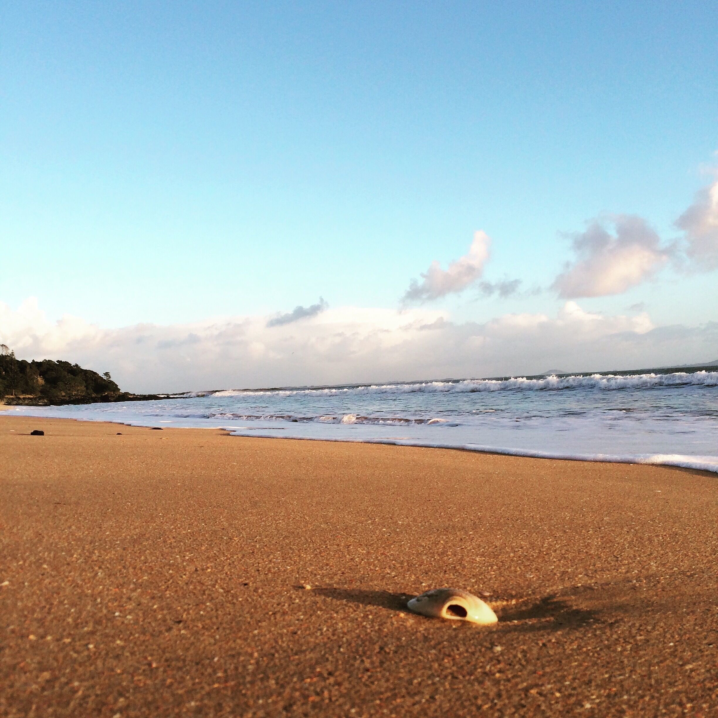 Uma praia arenosa com ondas suaves e céu claro.