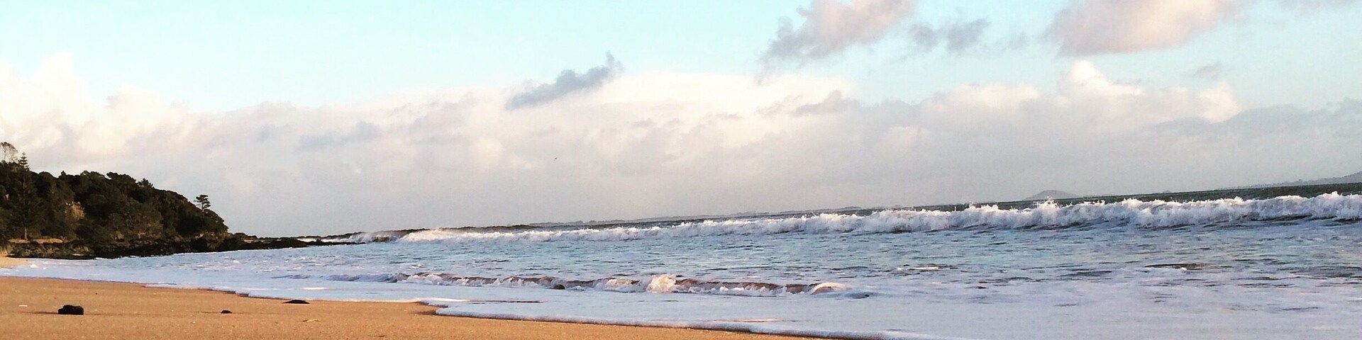 Uma praia arenosa com ondas suaves e céu claro.